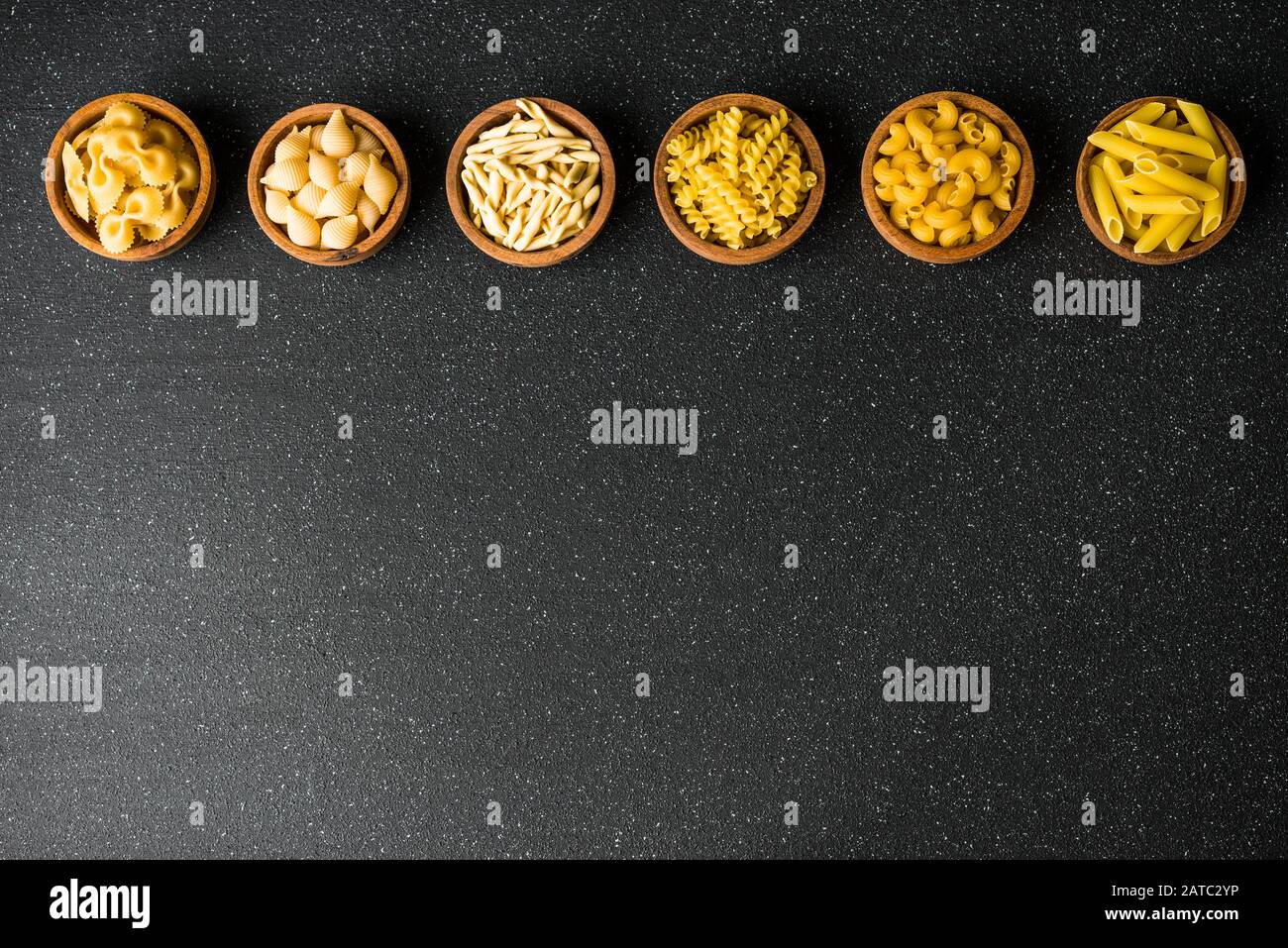 Assortment of different dry pasta types against black background, top ...