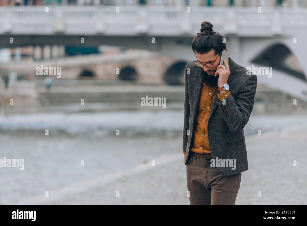 Young modern businessman talking on a phone at the city river walkway ...