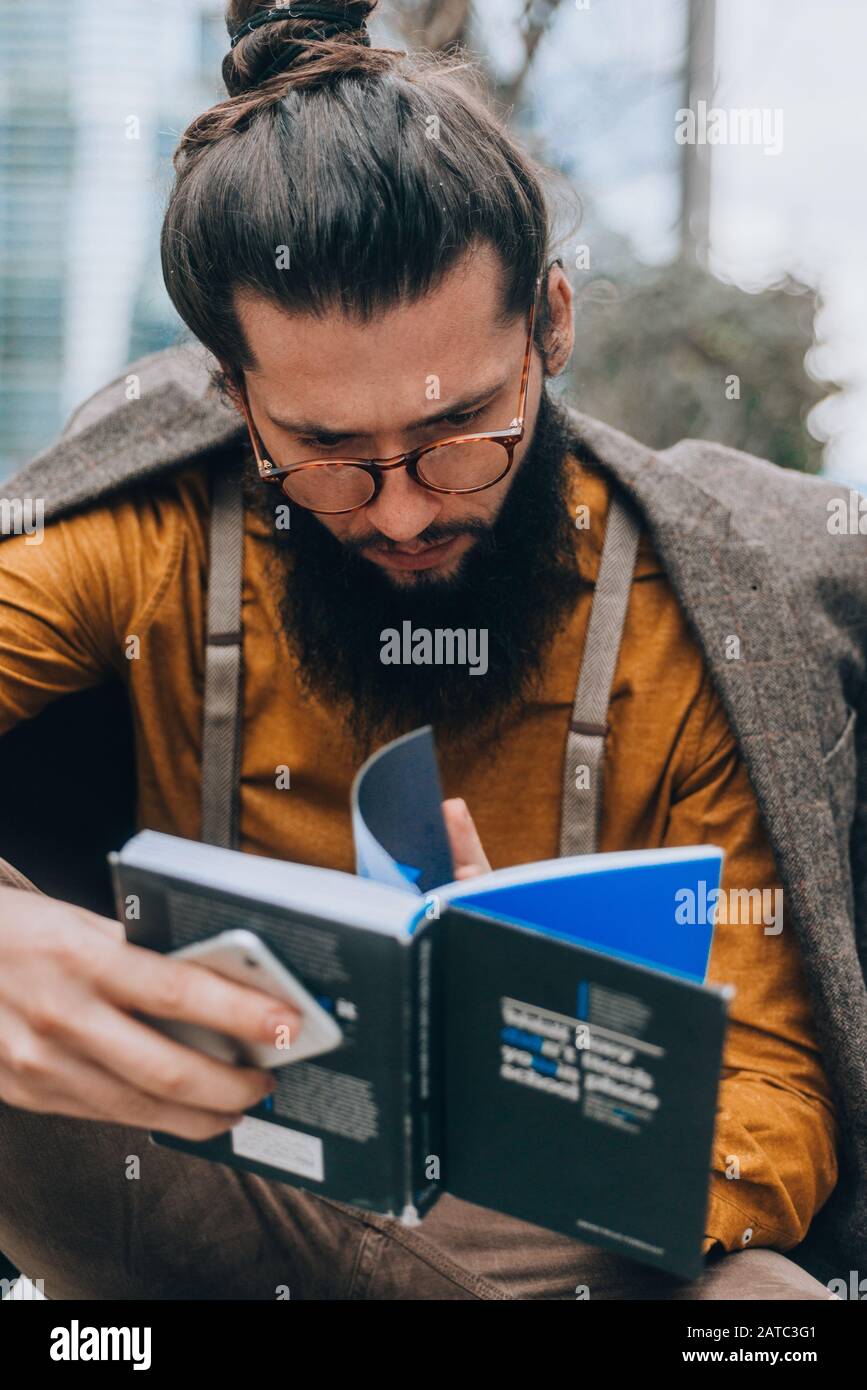 Modern day hipster reading a book at the city square during daytime ...