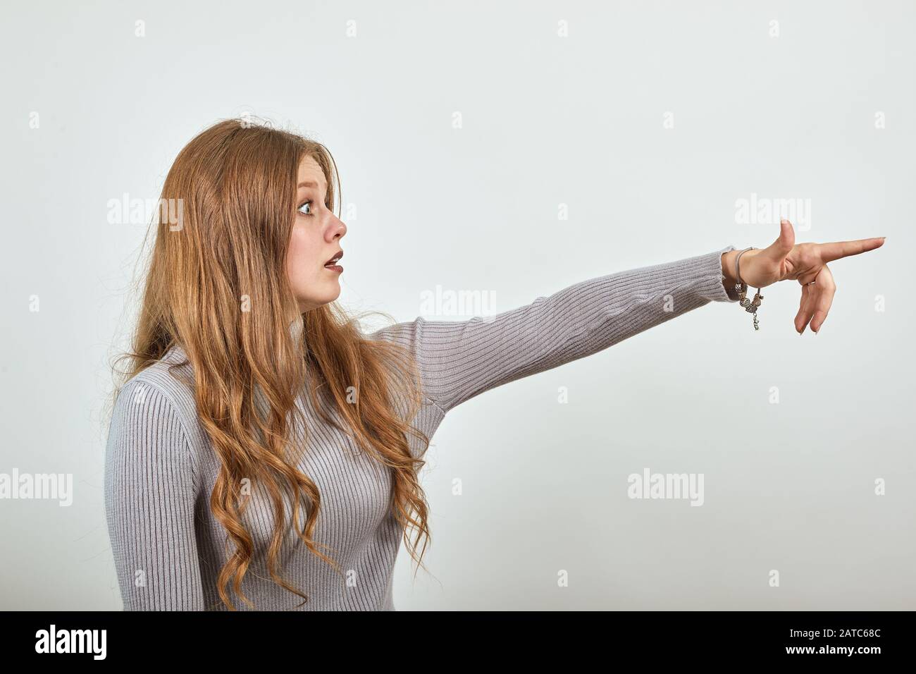 woman with red hair and gray sweater points index finger in frightened ...