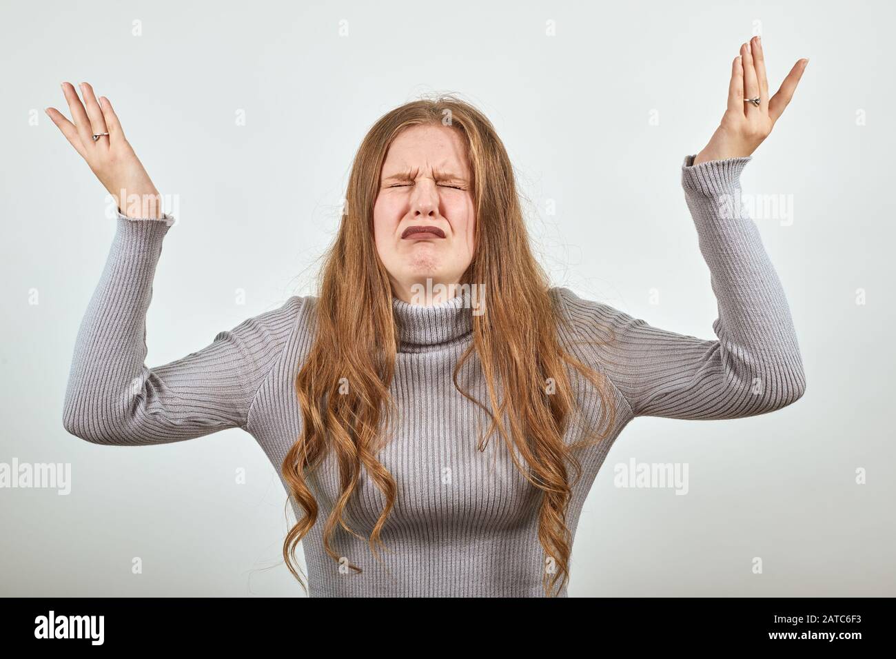 A young unhappy woman with red hair raises her hands in despair and ...