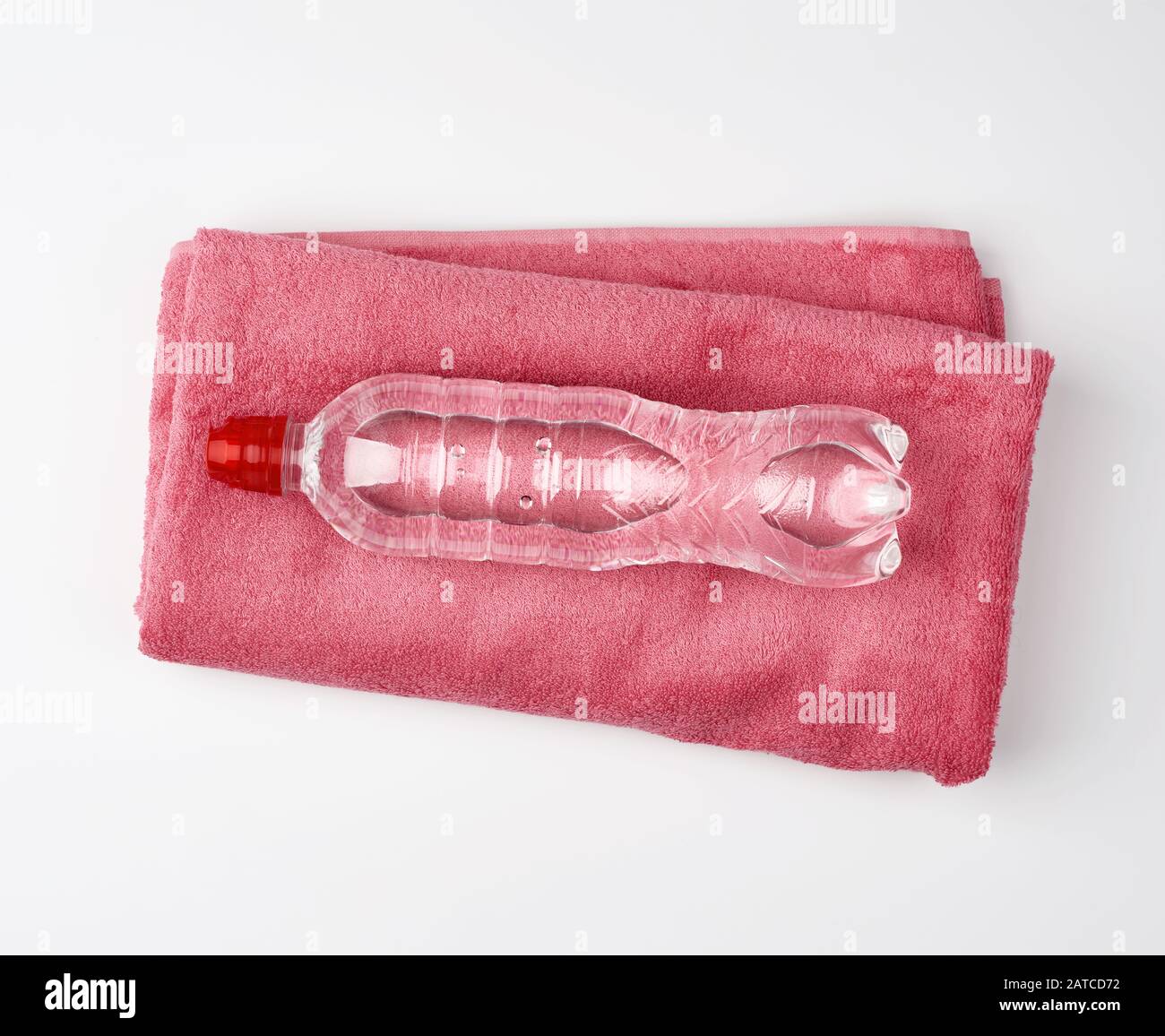 folded pink terry towel and a transparent bottle of water on a white ...
