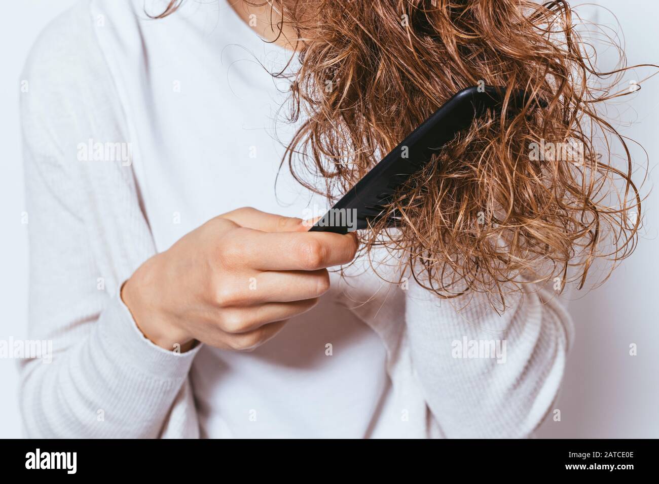Young woman wearing white shirt combing her tangled curly hair, close ...