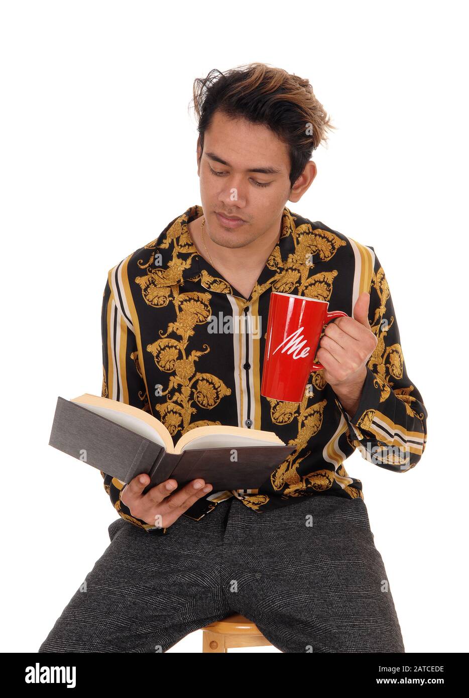 A tall young man sitting on a chair in the studio, reading his book and ...
