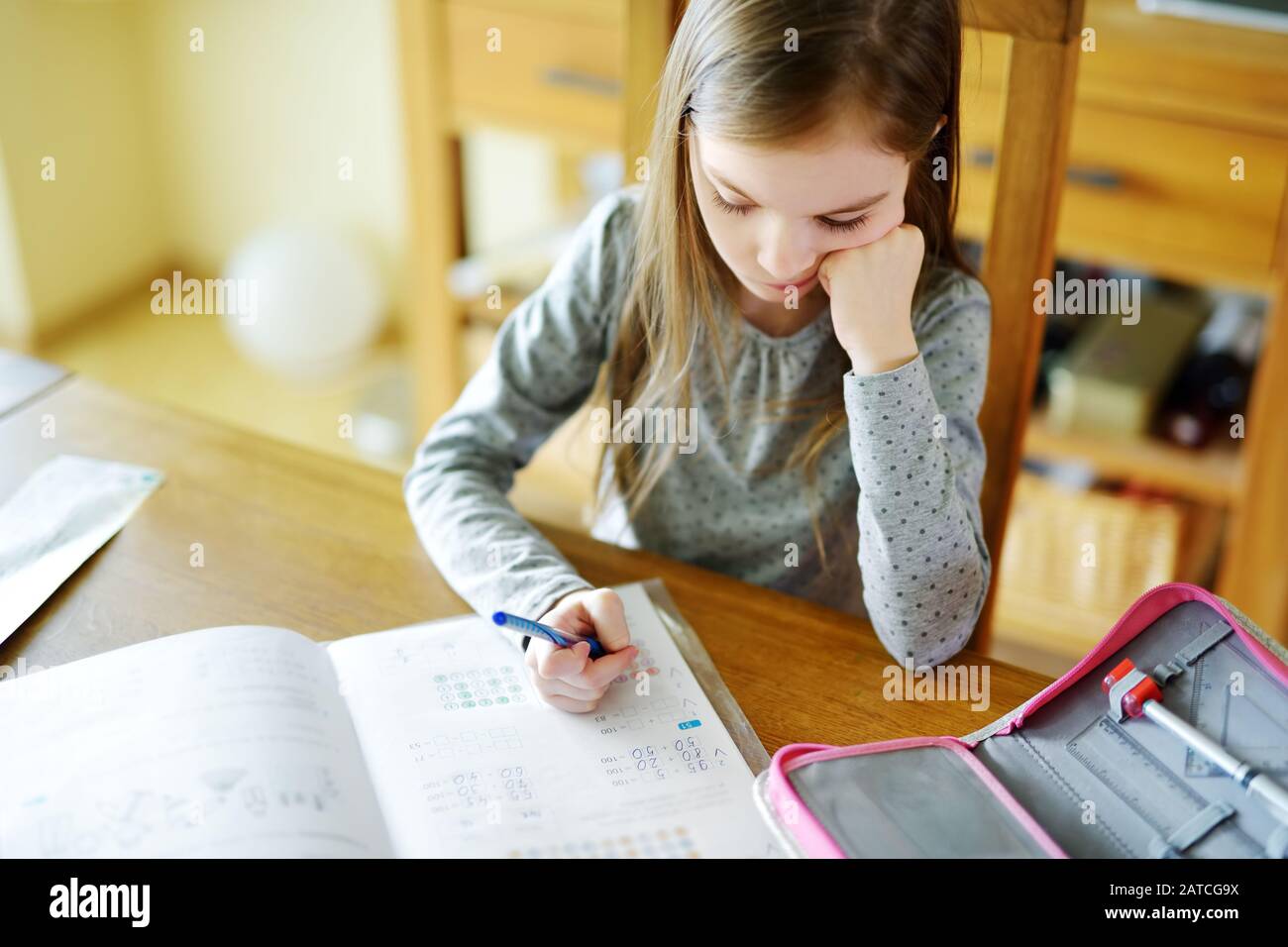 Smart little schoolgirl doing her homework at her table at home. Child ...