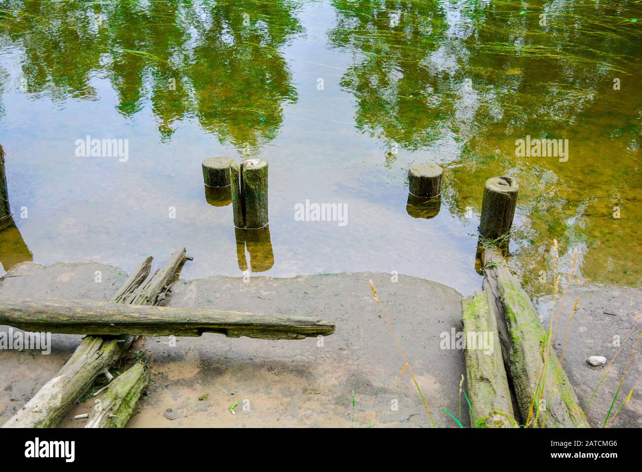 Sandy shore and old weathered wooden posts in reflective water of ...