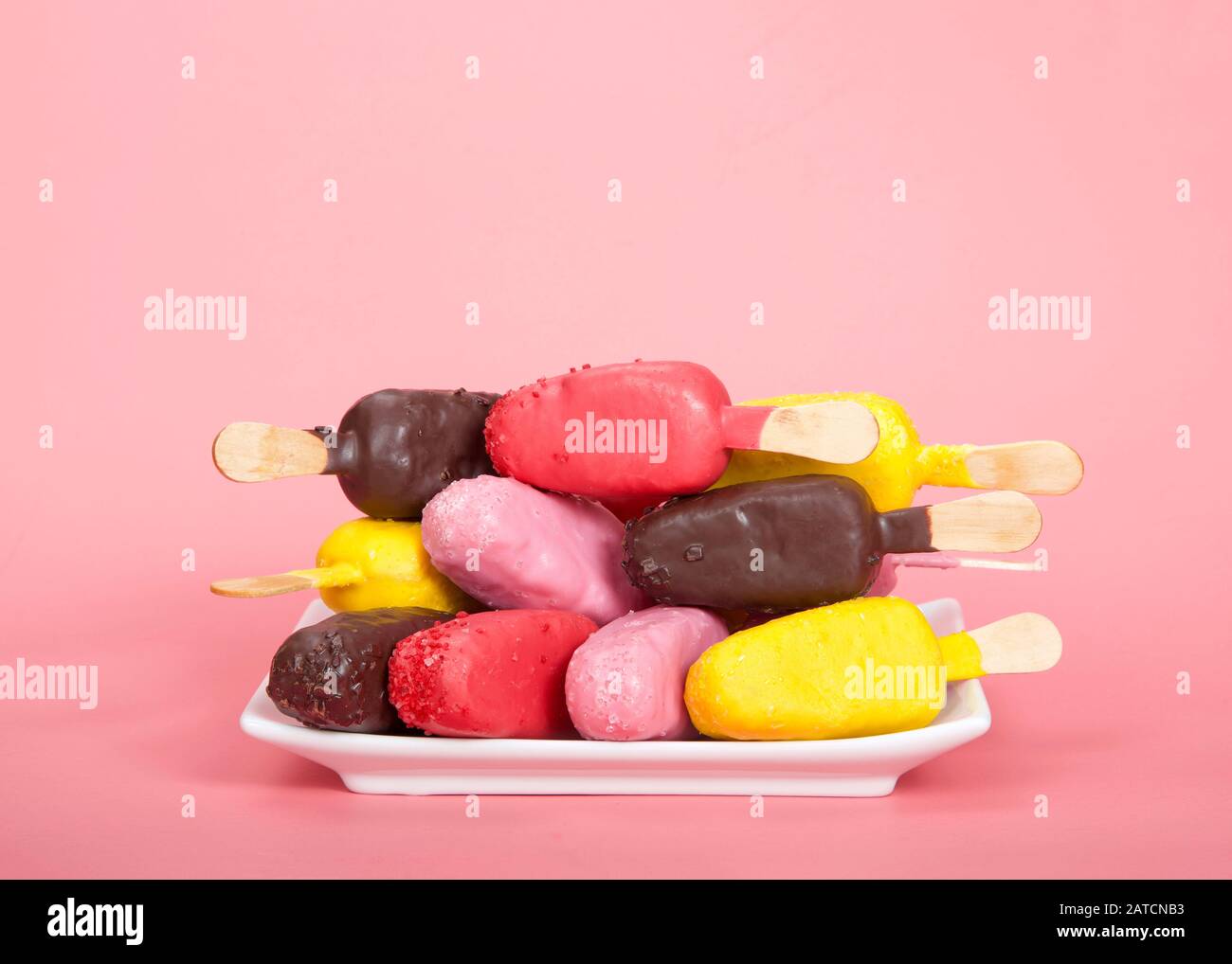 Colorful candy covered cake popsicles on a white plate alternating ...