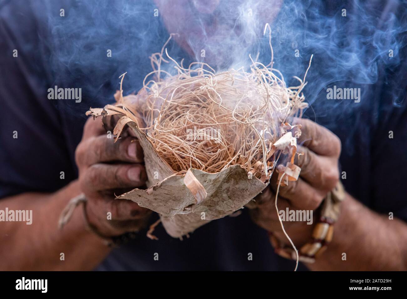 Closeup of man hand carrying burning smoky straw fire start on textured ...