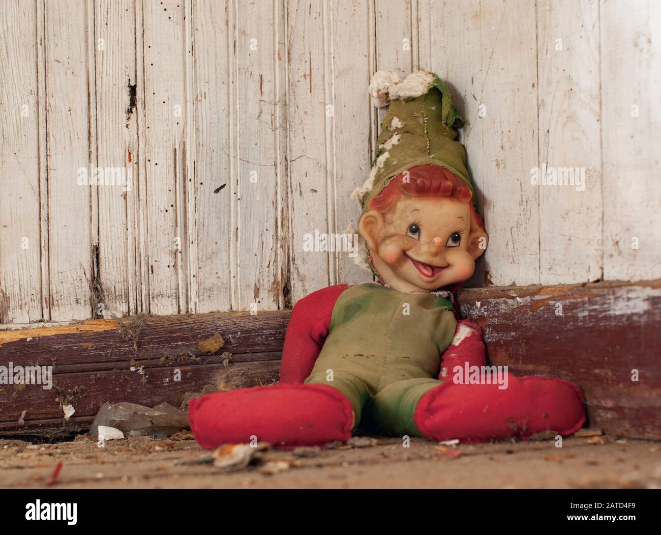 A raggedy, tattered, old red and green elf doll in a run down abandoned ...