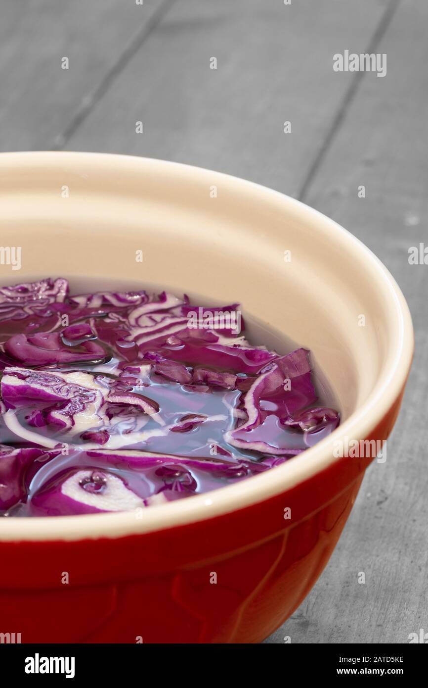 Sliced red cabbage soaking in water in a ceramic bowl. With a grey wood ...