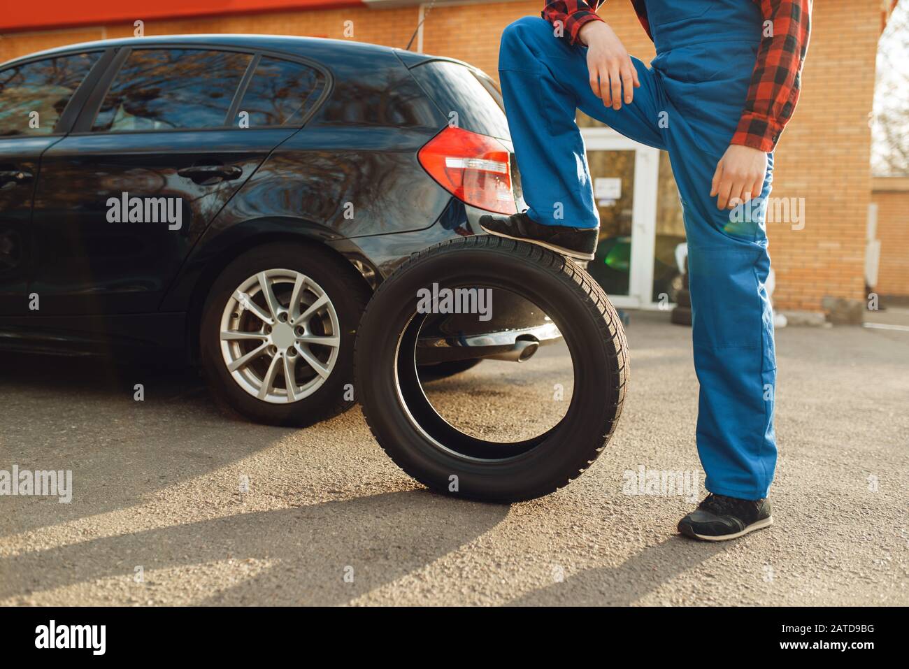 Worker in uniform poses with tyre, tire service Stock Photo - Alamy