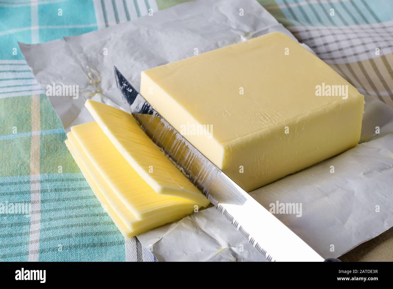 Knife cutting slices of fresh yellow butter from a just opened pack on ...