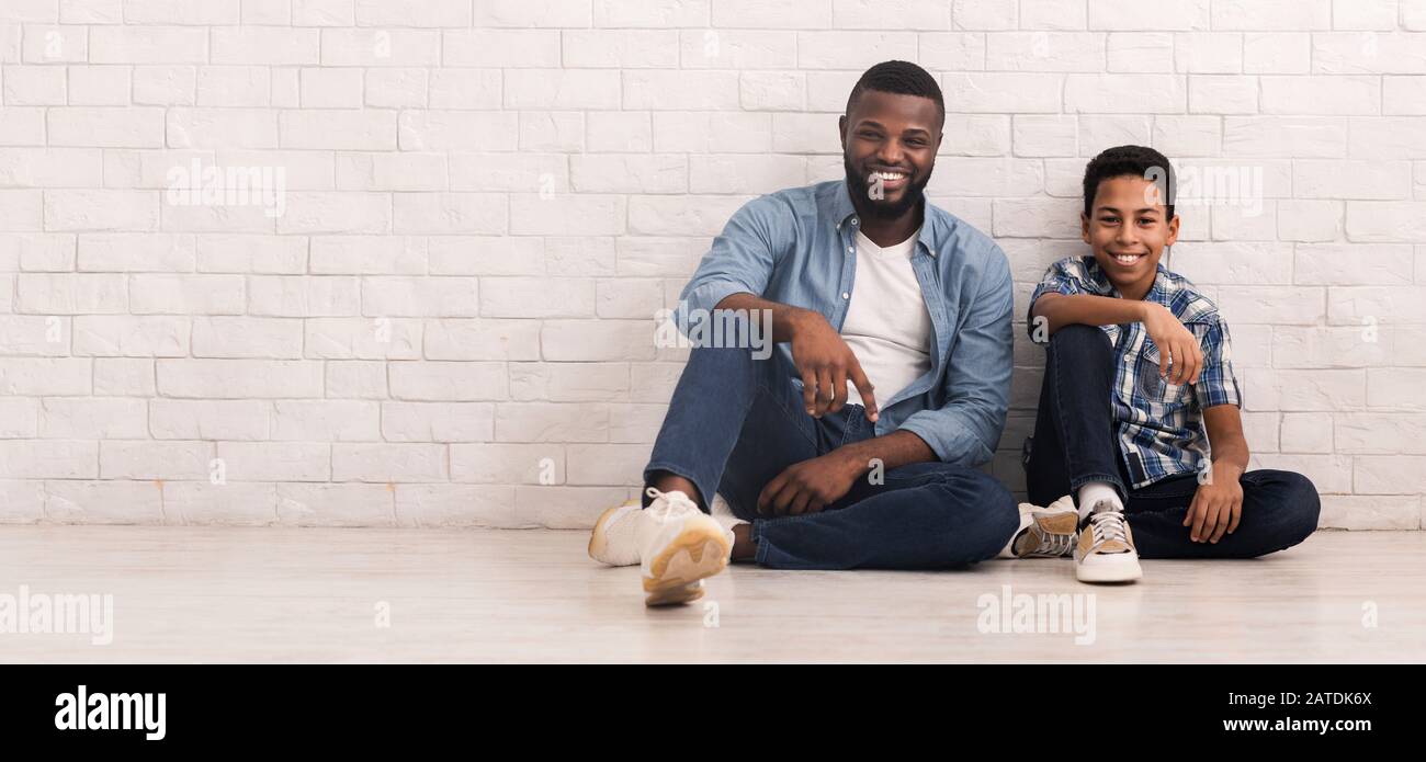 Happy afro father and son sitting on floor in similar pose Stock Photo ...