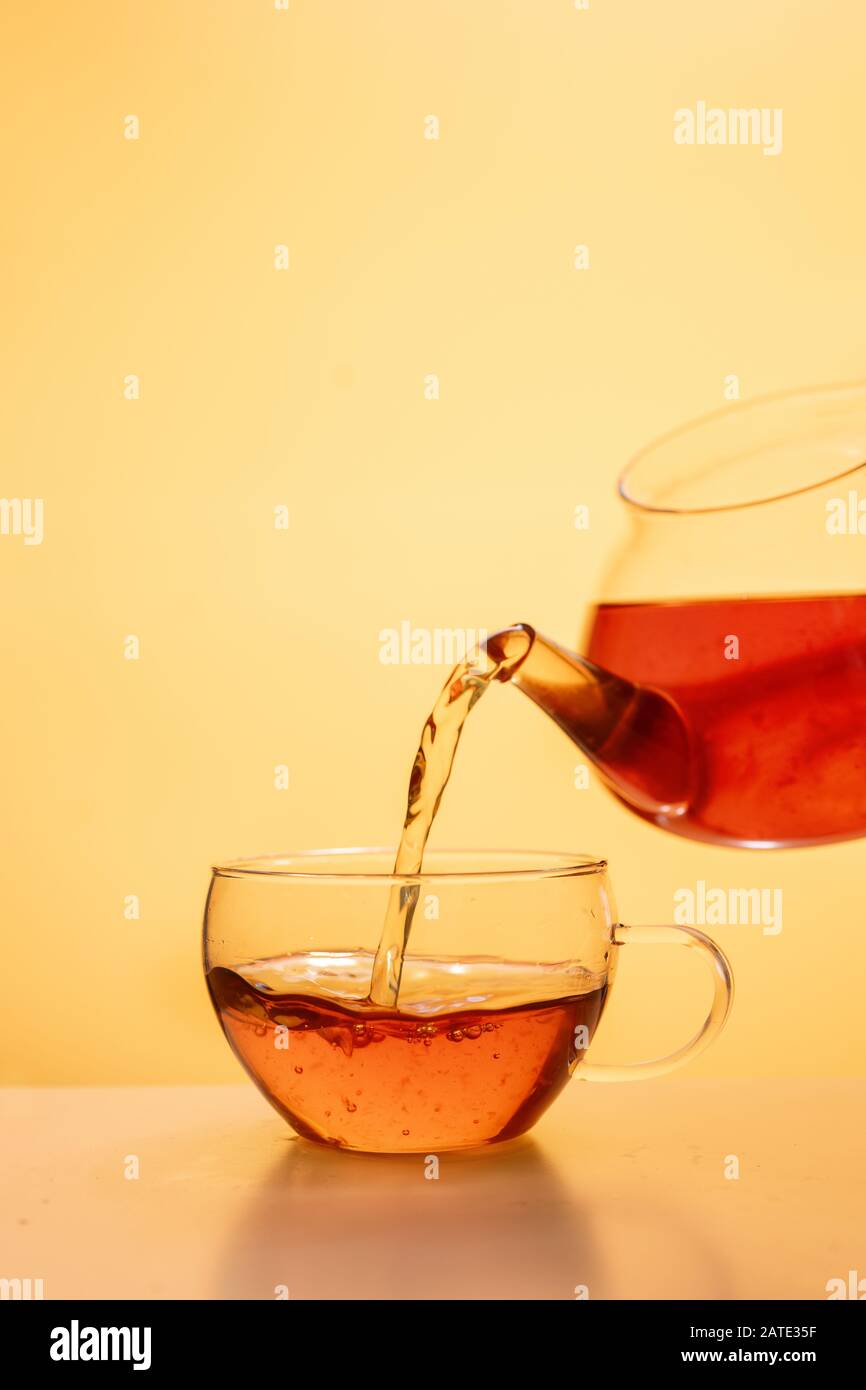 Tea being poured into glass tea cup against coral background Stock ...