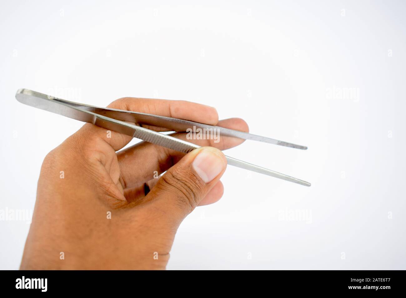 A person holding a tweezers with his fingers before a white background ...