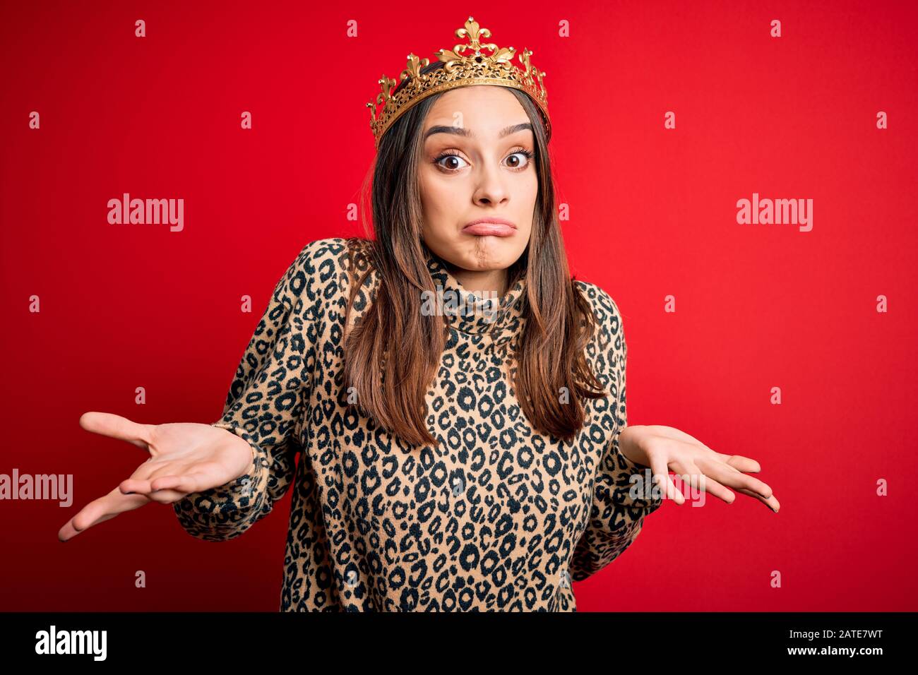 Young beautiful brunette woman wearing golden crown queen over isolated ...