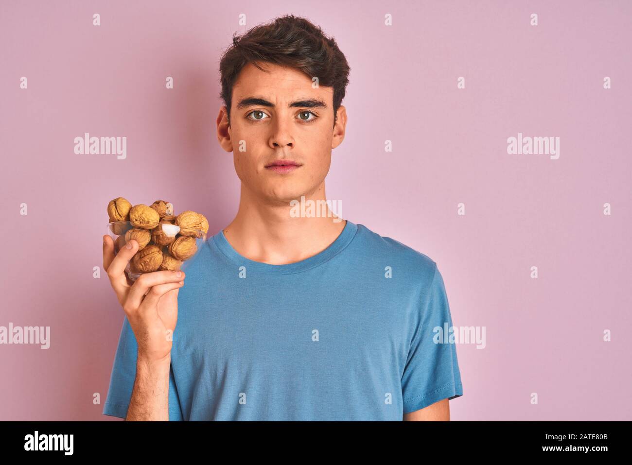 Teenager boy holding bunch of natural walnuts over pink isolated ...