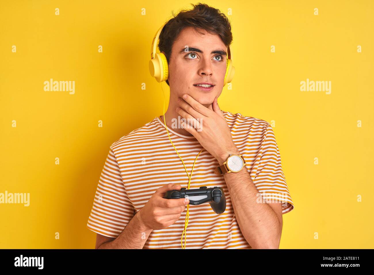 Teenager boy playing video games using gamepad over isolated yellow ...