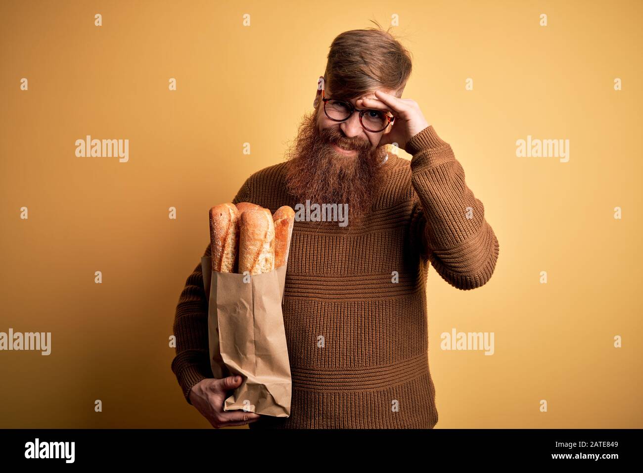 Irish Redhead Man With Beard Holding Groceries Paper Bag Of Bread Over Yellow Background