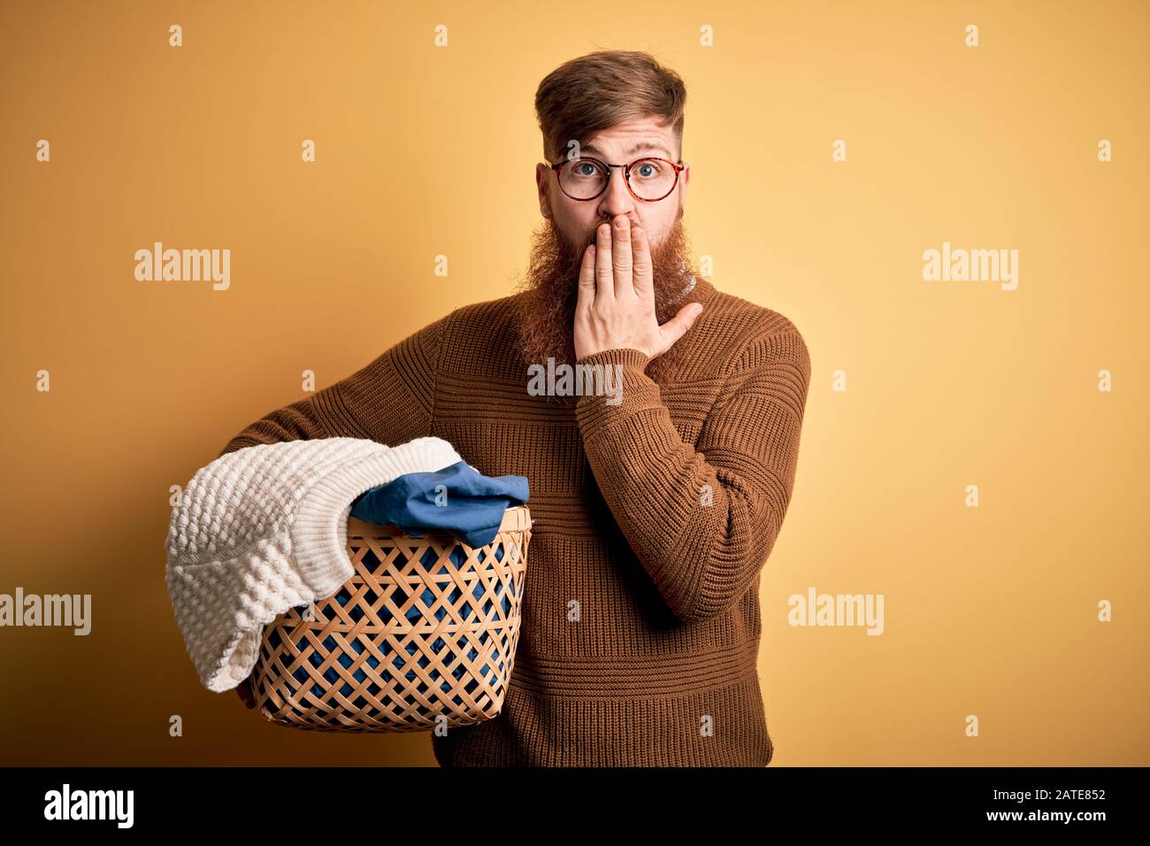 Redhead Irish Man With Beard Doing Housework Laundry Over Yellow Background Cover Mouth With