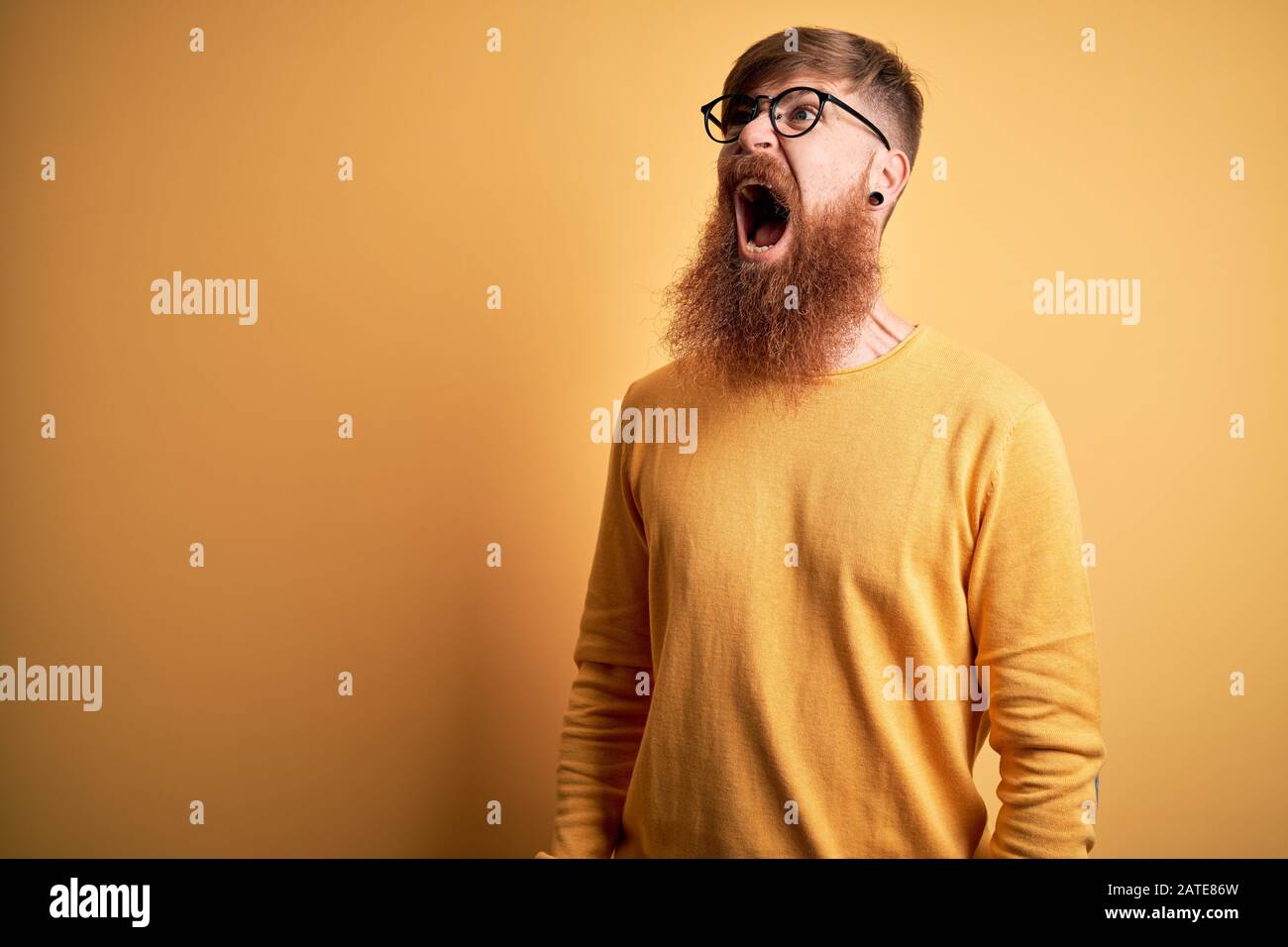 Handsome Irish redhead man with beard wearing glasses over yellow ...