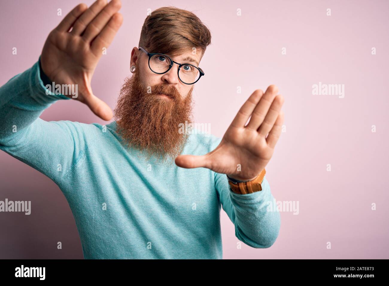 Handsome Irish redhead man with beard wearing glasses over pink ...