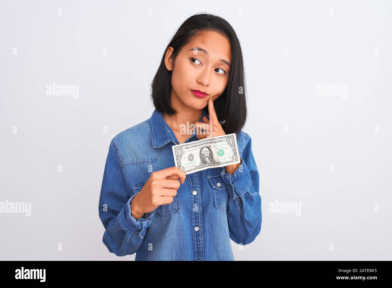 Young beautiful chinese woman holding one dollar standing over isolated ...