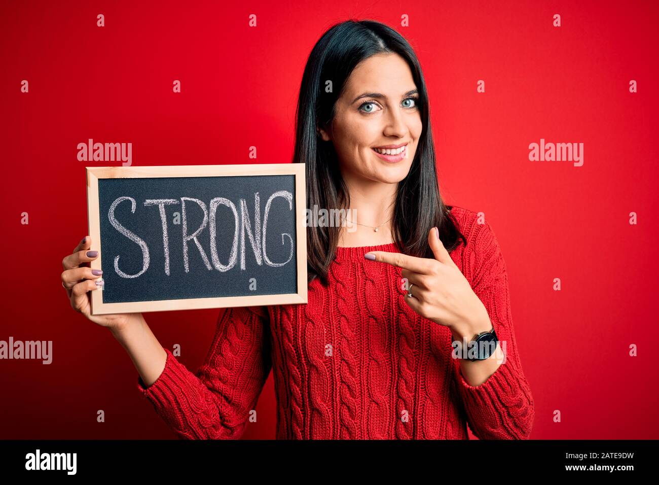 Young brunette woman with blue eyes holding blackboard with strong word ...