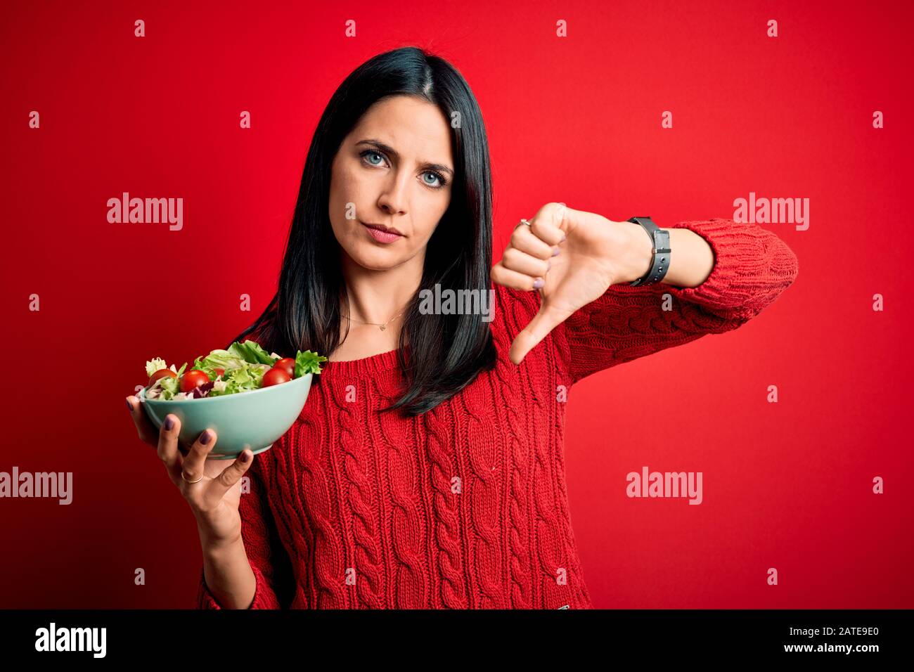 Young brunette woman with blue eyes eating healthy green salad over ...
