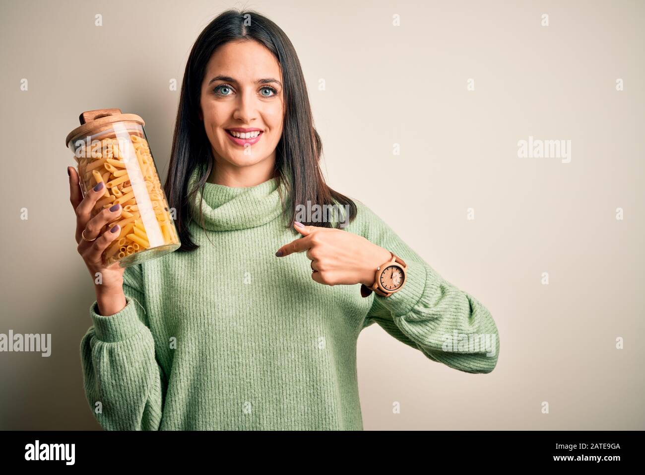 Young brunette woman holding dry italian macaroni over brown isolated ...