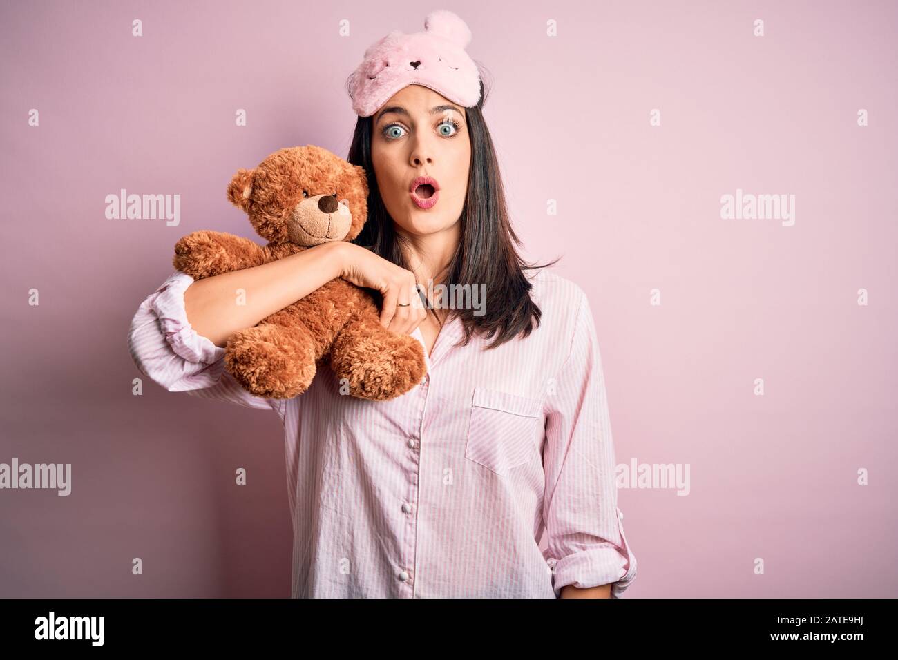 Young brunette woman with blue eyes wearing pajama hugging teddy bear ...