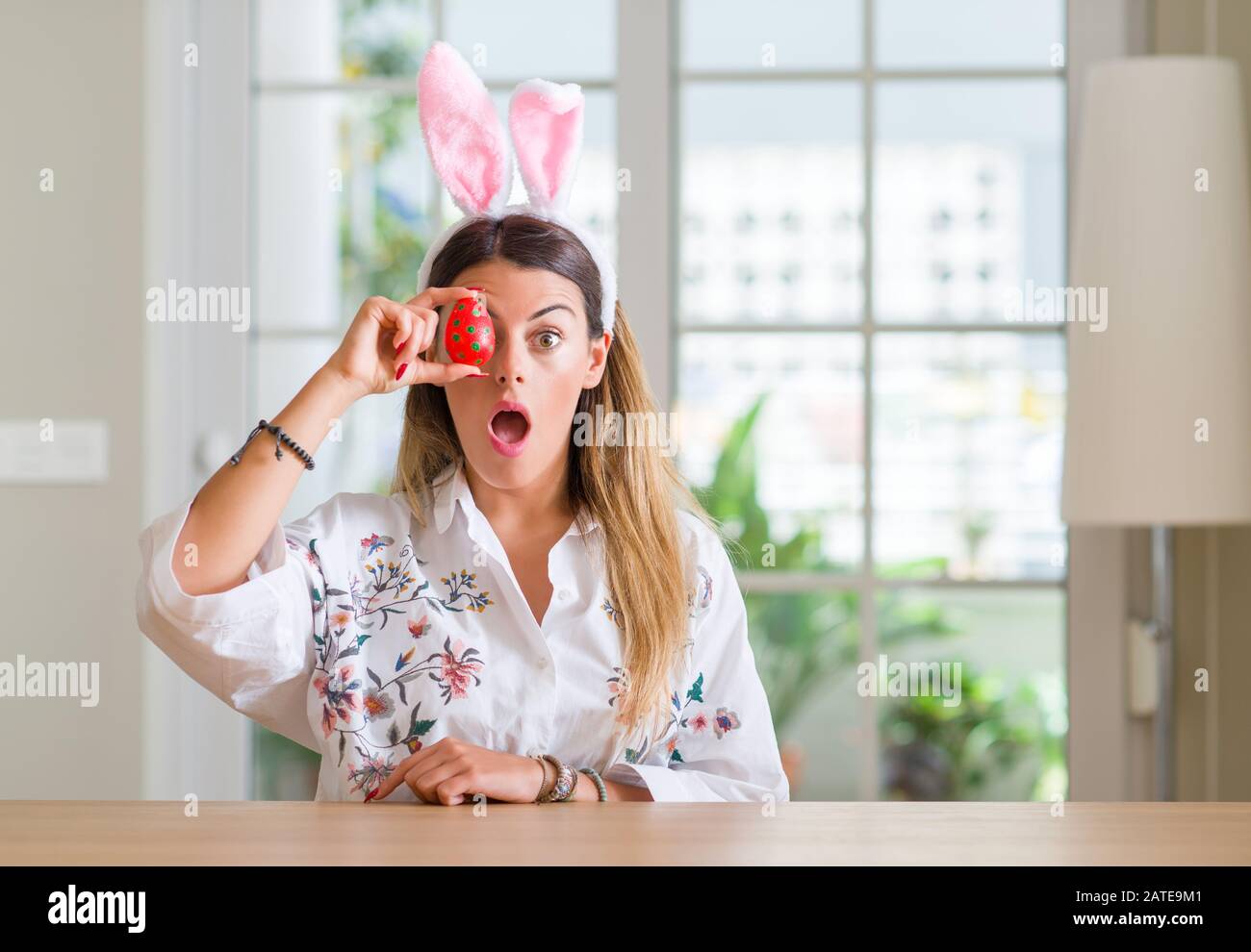 Young woman at home wearing easter rabbit ears scared in shock with a ...