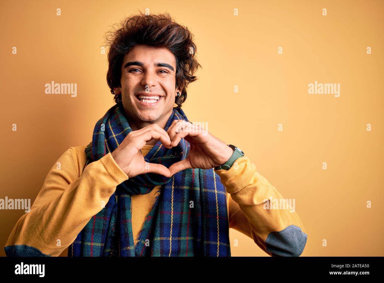 Young handsome man wearing casual scarf standing over isolated yellow ...