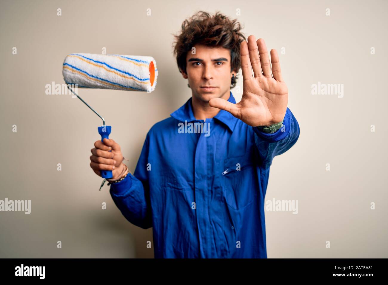 Young handsome painter man holding roller wearing uniform over isolated ...