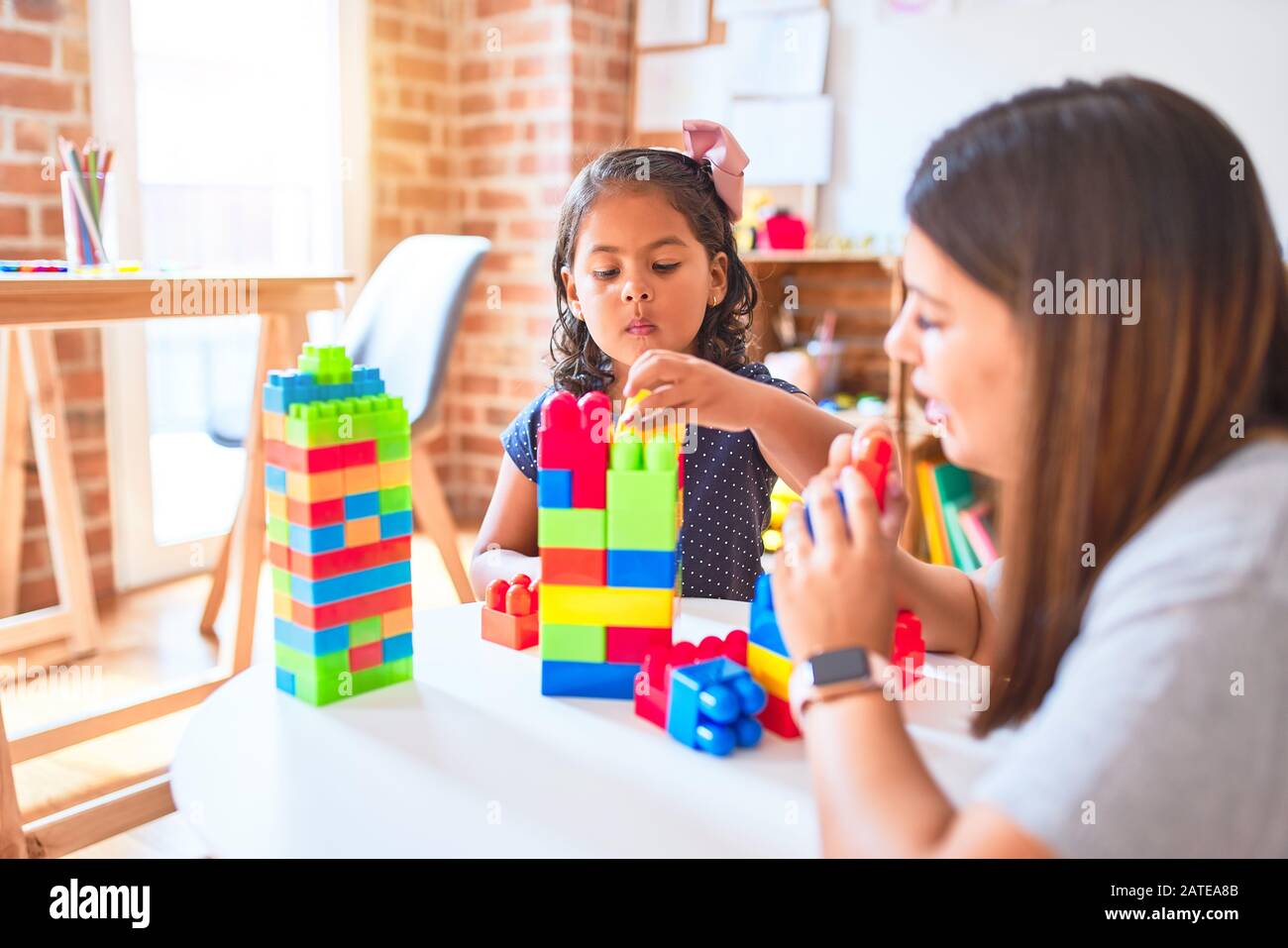 Beautiful teacher and toddler girl playing with construction blocks ...