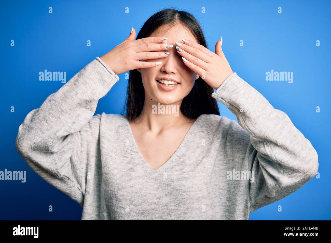 Young beautiful asian woman wearing casual sweater standing over blue ...