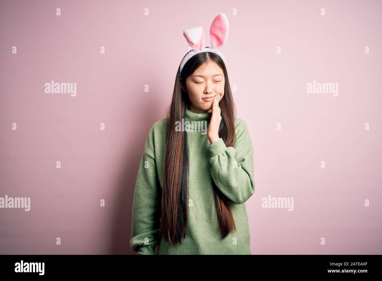 Young asian woman wearing cute easter bunny ears over pink background ...