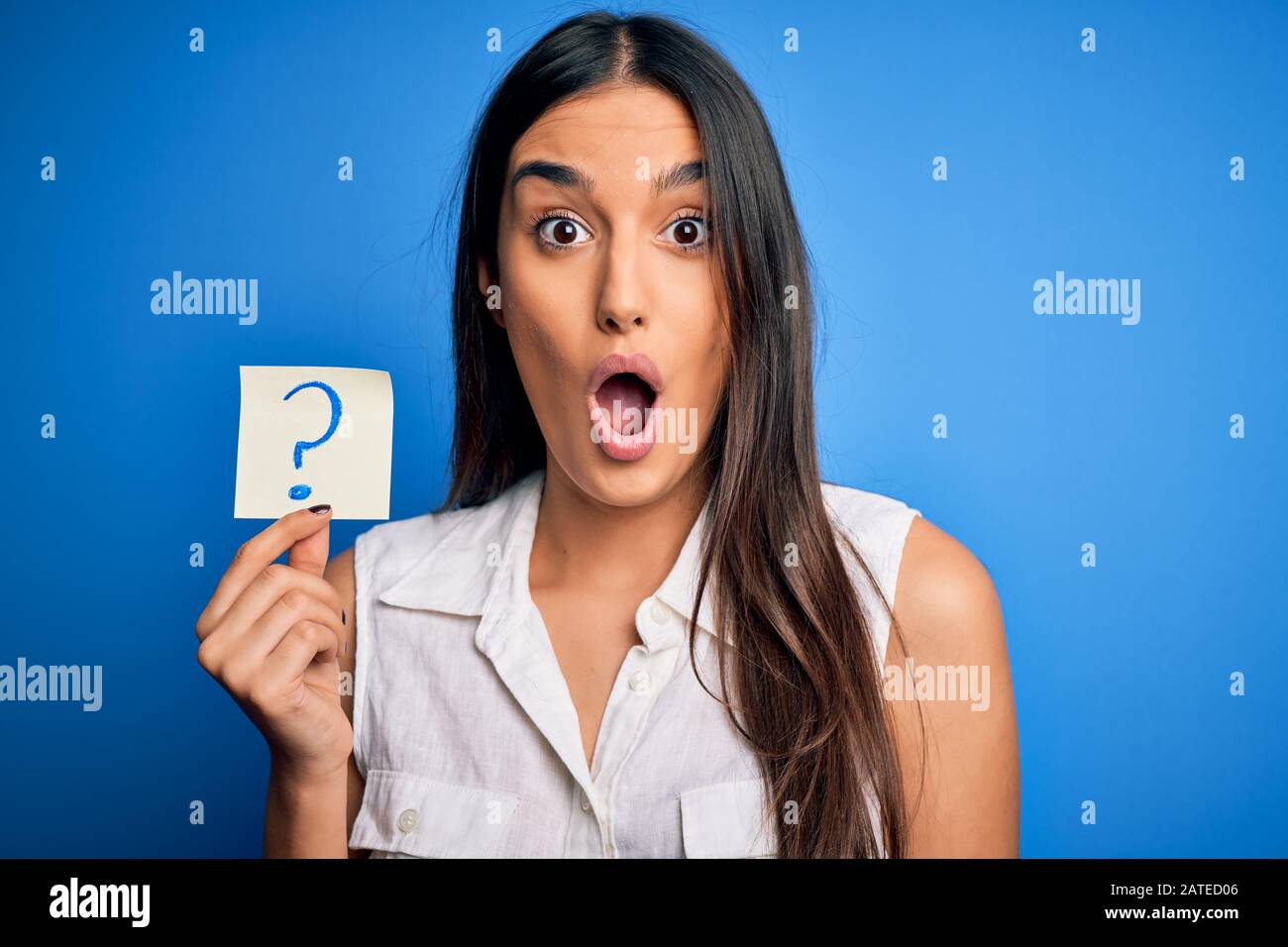 Young beautiful brunette woman holding paper with question mark symbol ...