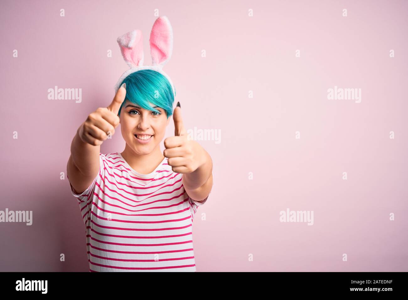 Young woman with fashion blue hair wearing easter rabbit ears over pink ...