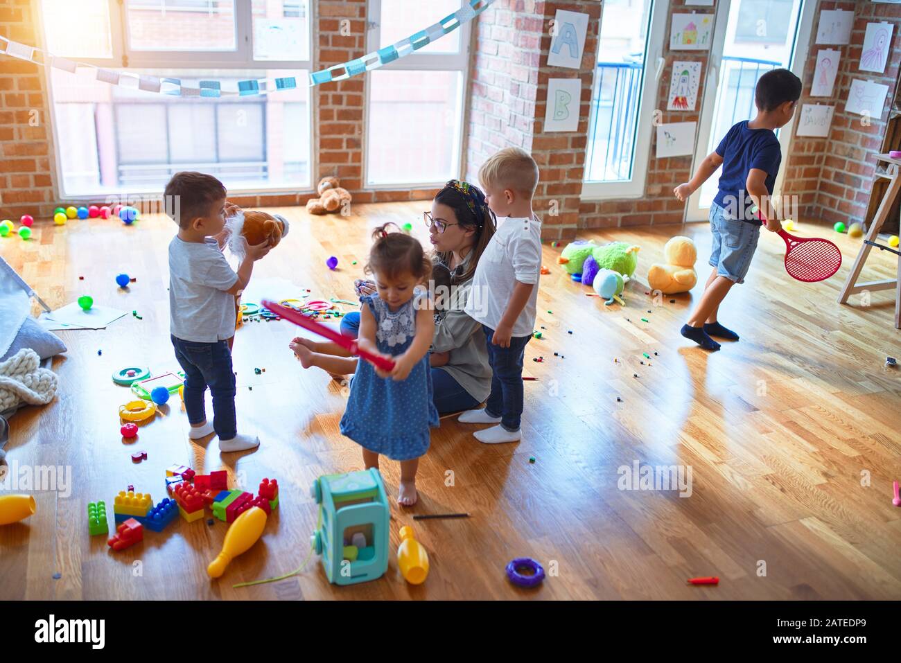 Beautiful teacher and group of toddlers playing around lots of toys at ...