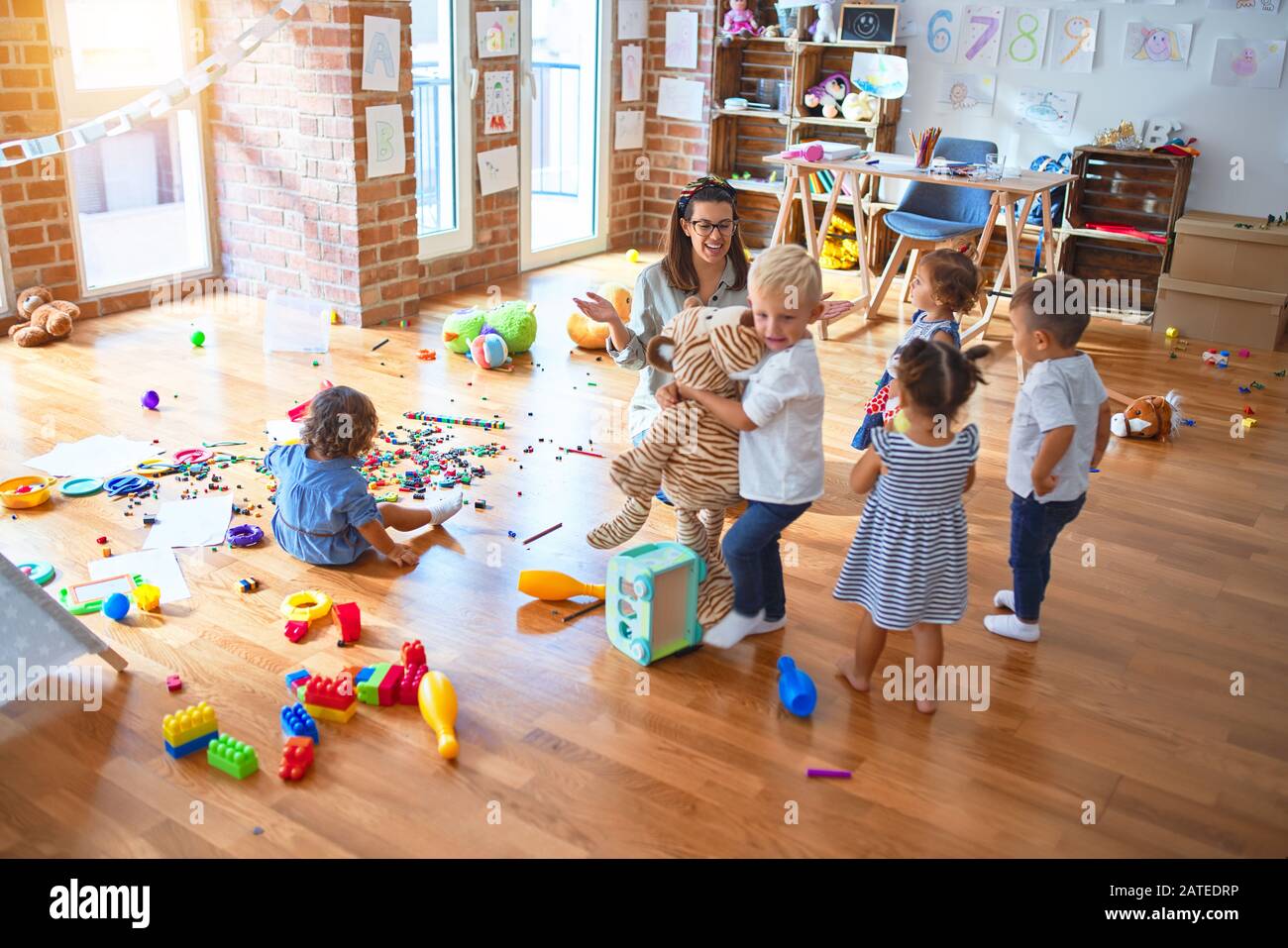 Beautiful teacher and group of toddlers playing around lots of toys at ...