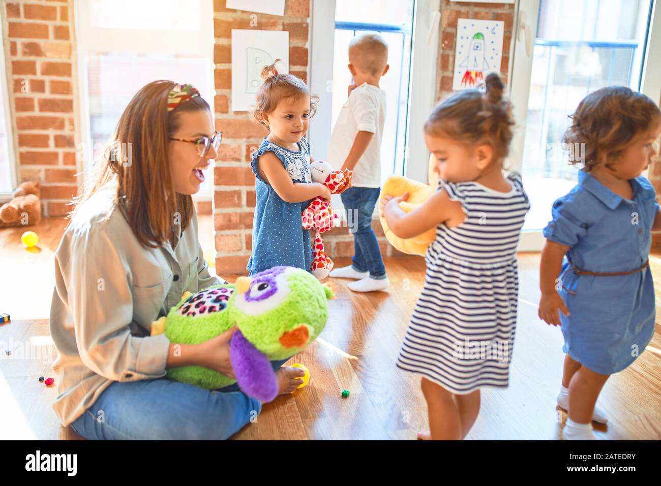 Beautiful teacher and group of toddlers playing around lots of toys at kindergarten Stock Photo ...
