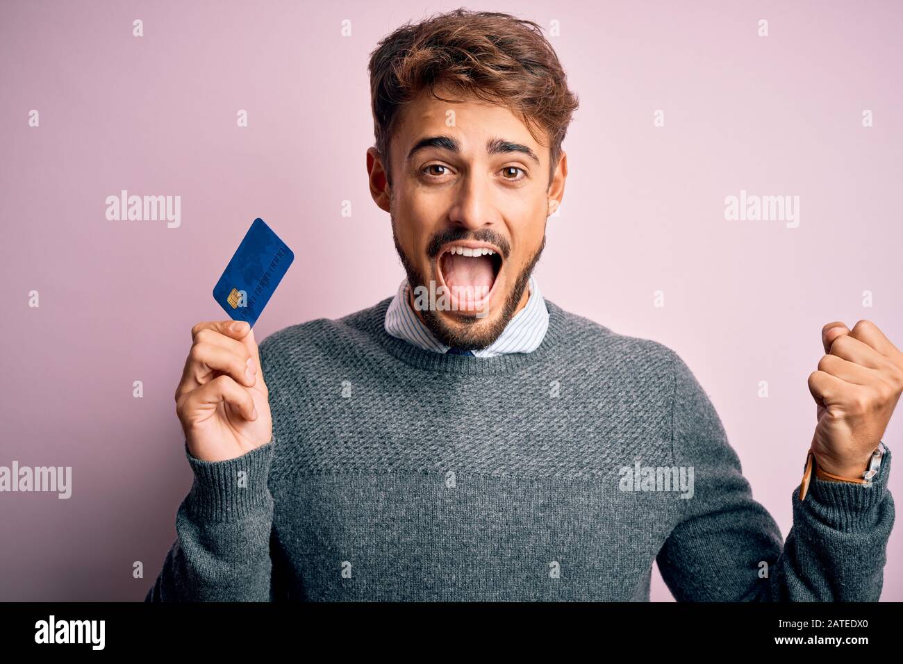 Young customer man with beard holding credit card for payment over pink ...