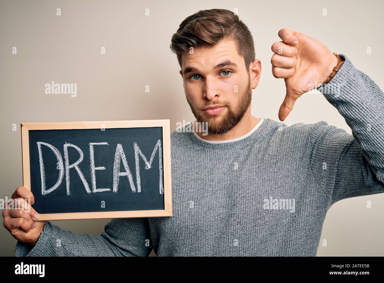 Young blond man with beard and blue eyes holding blackboard with dream ...