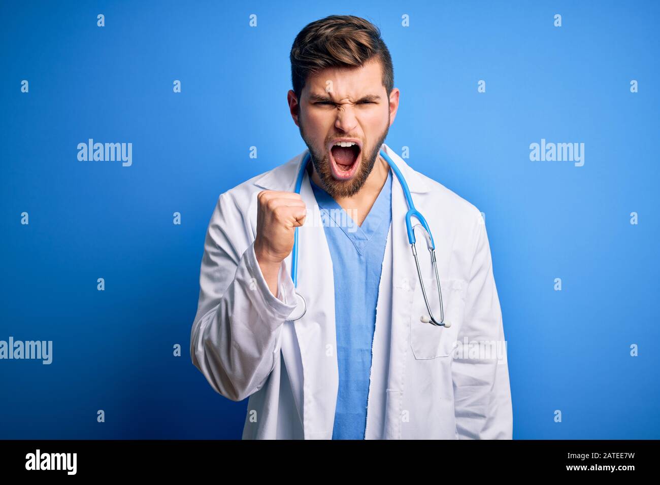 Young blond doctor man with beard and blue eyes wearing white coat and ...