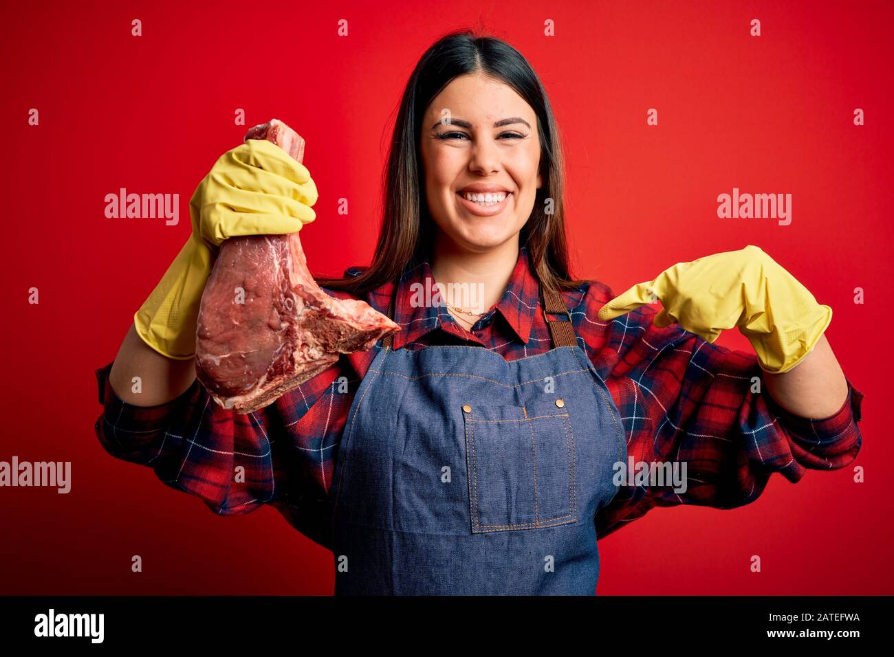 Young butcher woman holding fresh raw beef meat stake over red ...