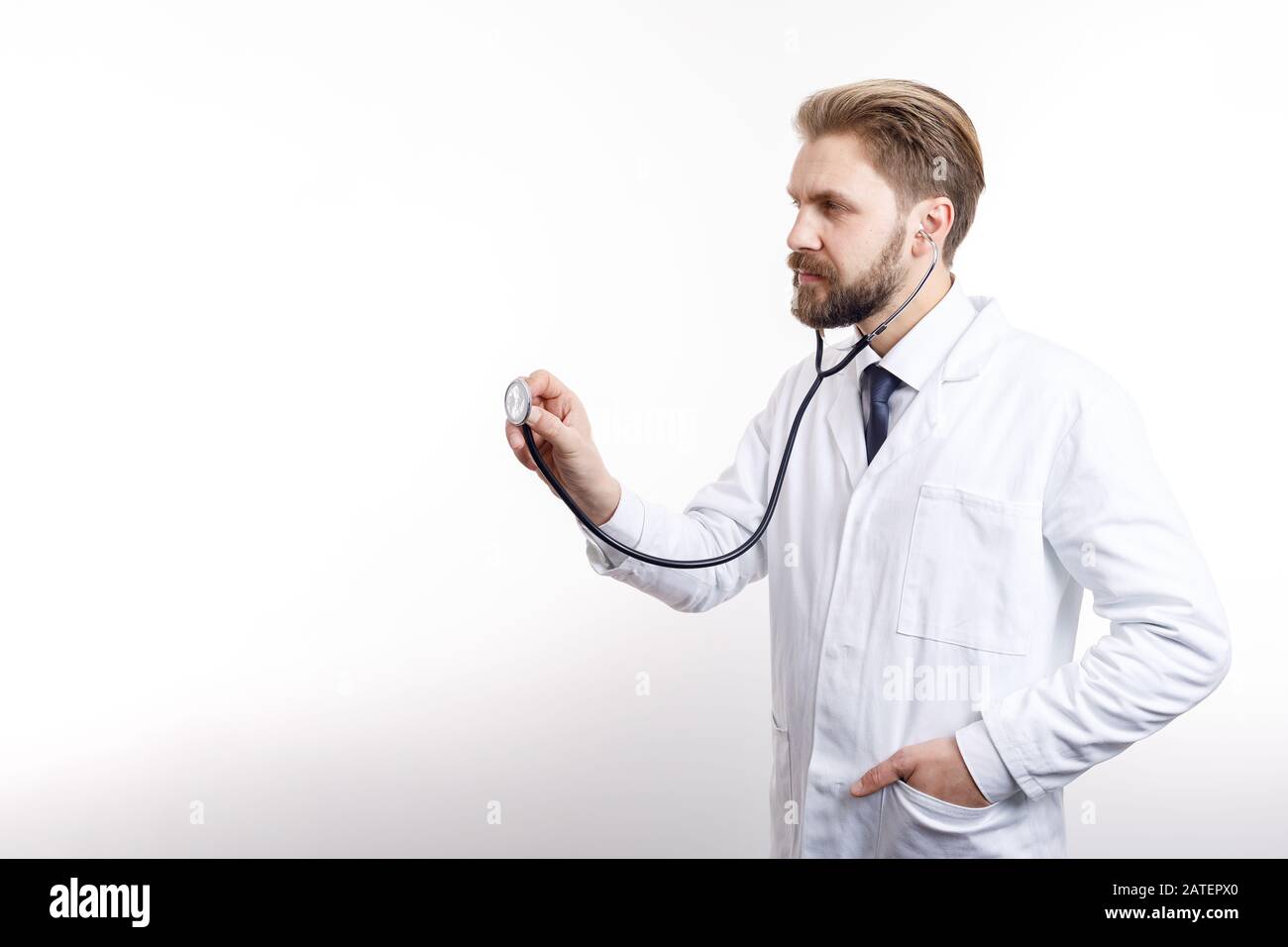 Pensive half-turned doctor in white coat posing as if auscultating ...