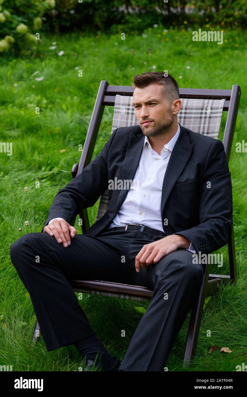 Handsome man in suit is sitting and listening in chair outdoors Stock ...