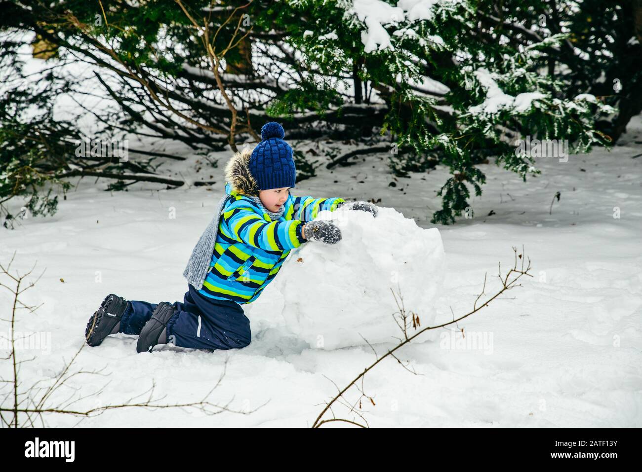 little cute boy making snowman. rolling big snowball Stock Photo - Alamy