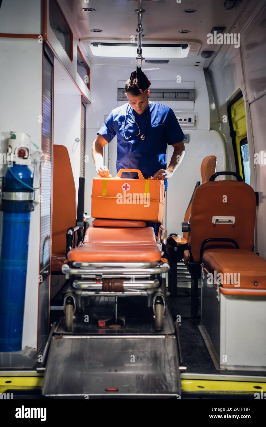 Young man in blue medical uniform packs medical bag in the ambulance ...